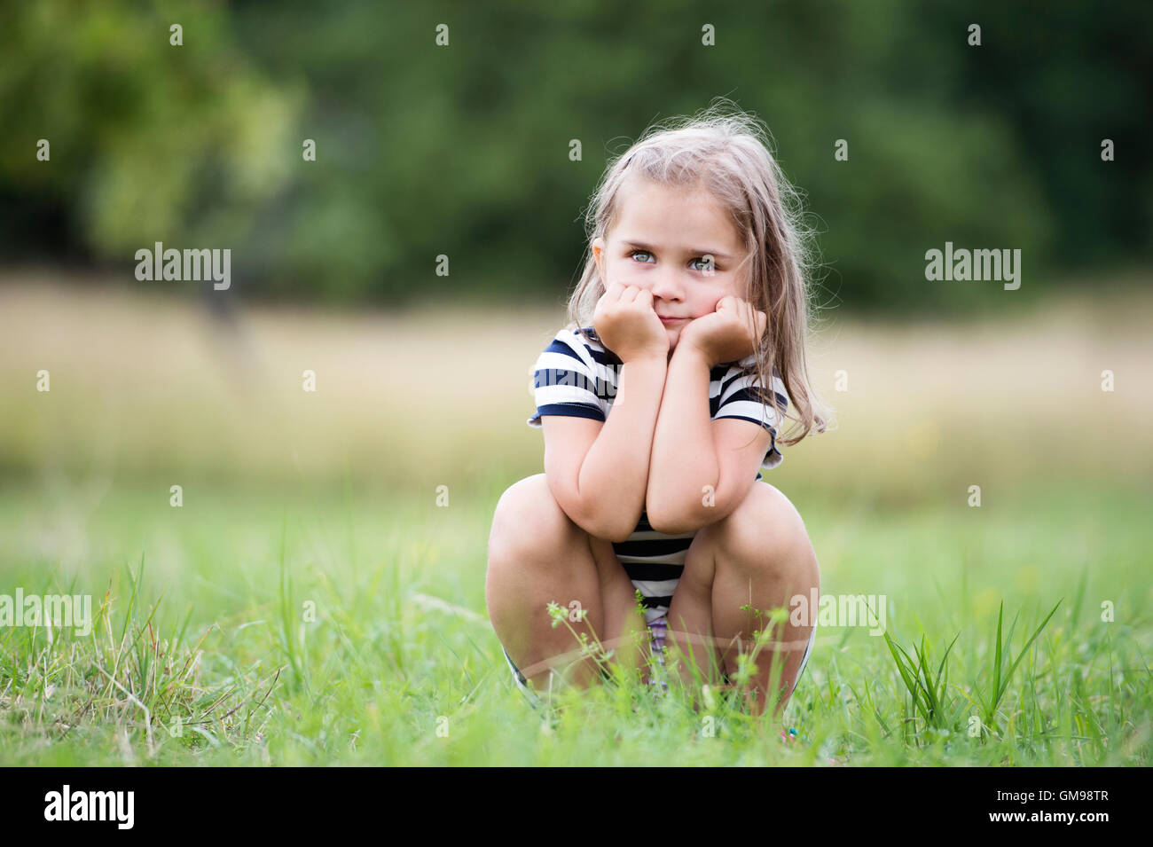Little girl crouching on a meadow Stock Photo - Alamy