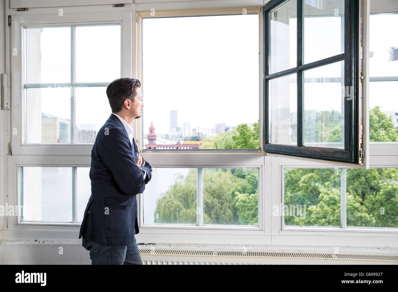 Businessman standing at open window with arms crossed Stock Photo - Alamy