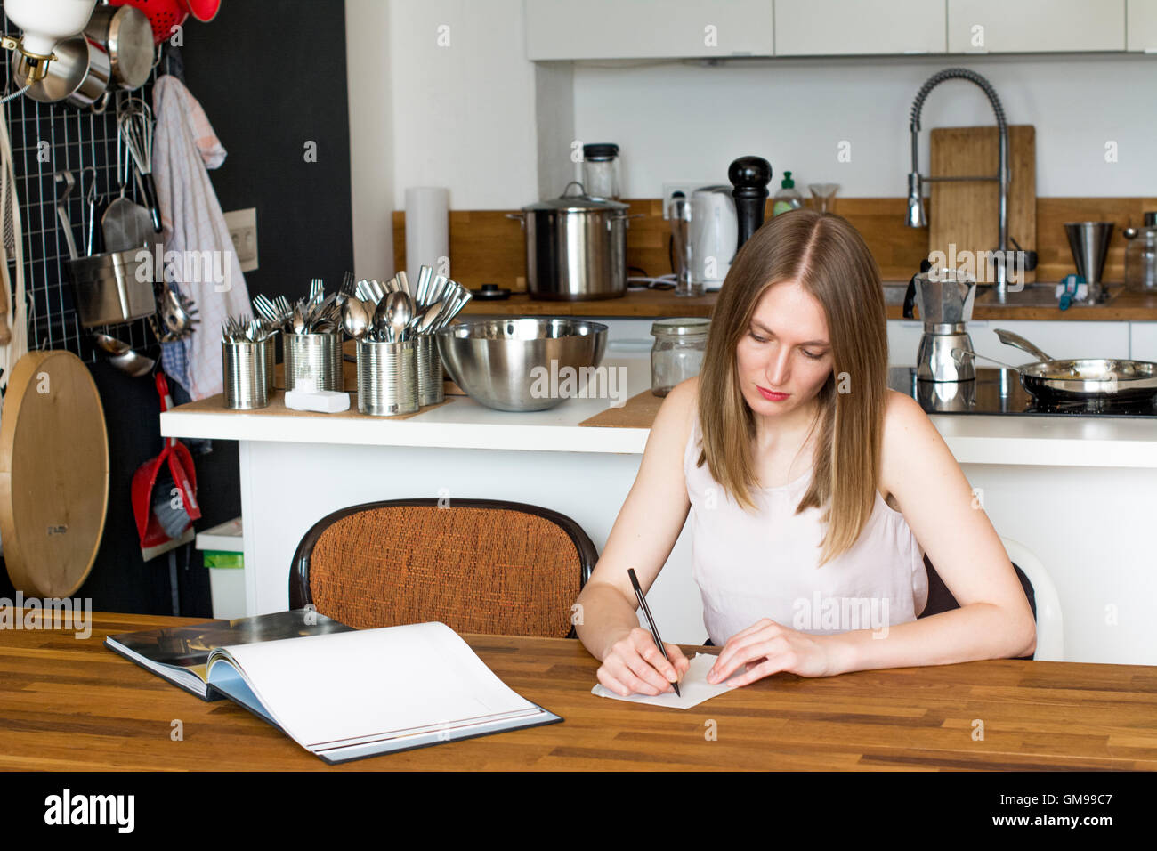 Woman sitting at table in her kitchen writing down something Stock ...