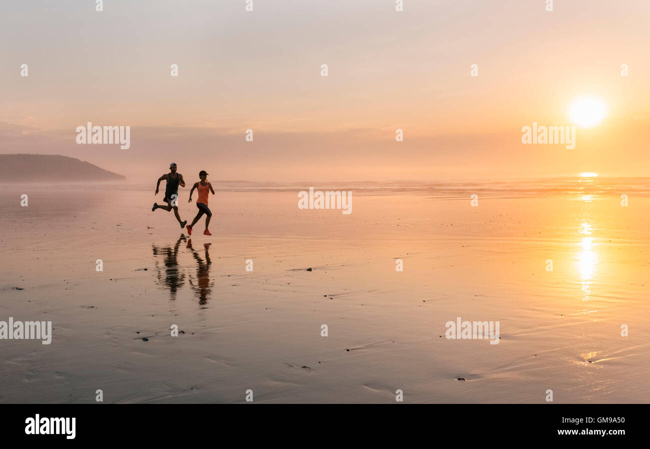 Athletes couple running on the beach at sunset Stock Photo - Alamy