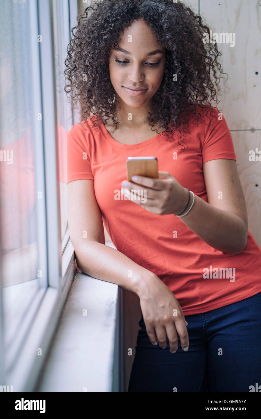 Young woman standing by window, using smart phone Stock Photo - Alamy