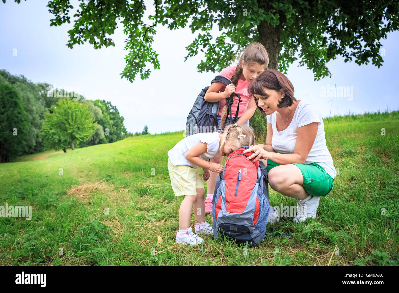 Mother and daughters on meadow during hiking, looking into backpack ...