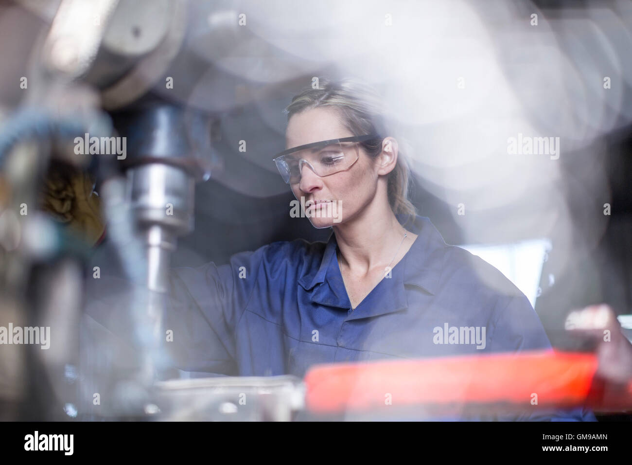 Female mechanic wearing safety goggles using drilling machine in ...