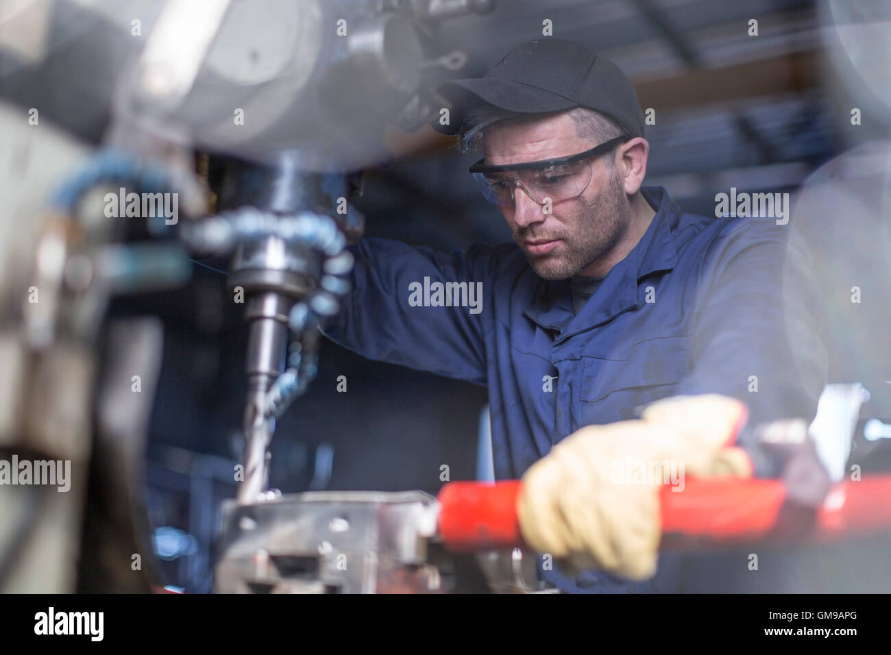 Mechanic wearing safety goggles using drilling machine in workshop ...