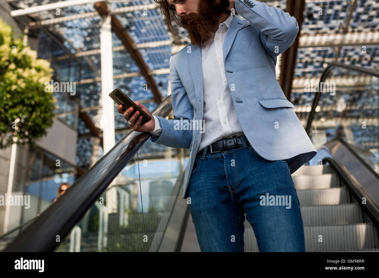 Stylish businessman using cell phone on escalator Stock Photo - Alamy