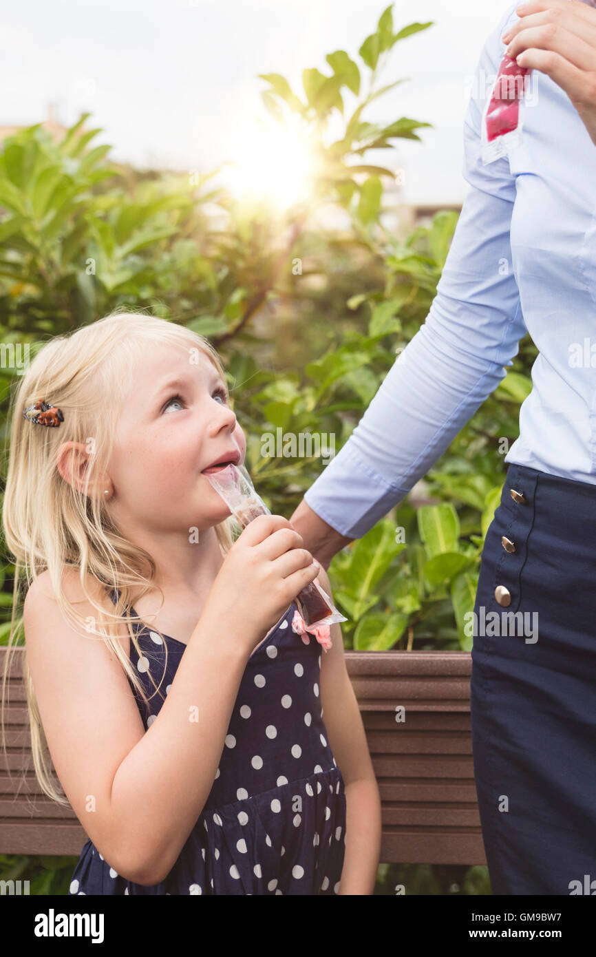 Little girl eating water ice looking at her mother Stock Photo - Alamy