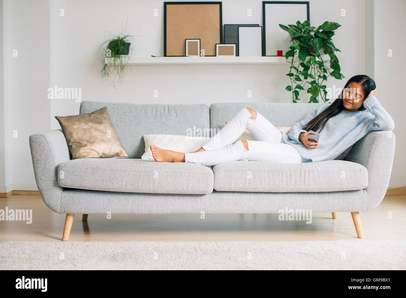 Young woman relaxing on couch in the living room using smartphone Stock ...