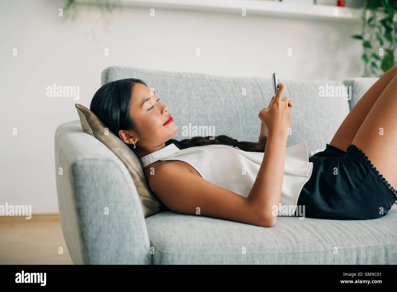 Young woman lying on couch using cell phone Stock Photo - Alamy