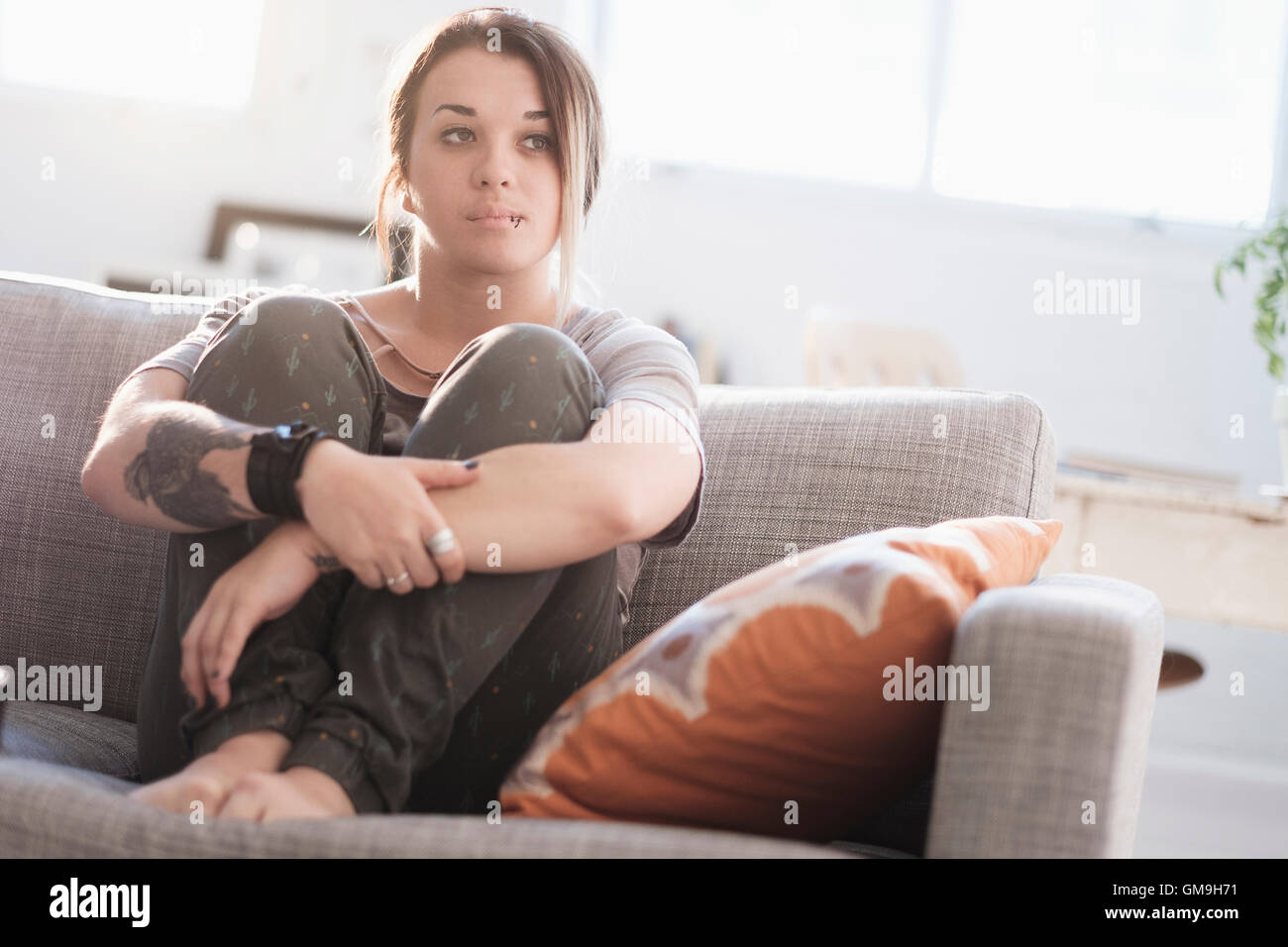 Sad woman sitting on sofa in living room Stock Photo - Alamy