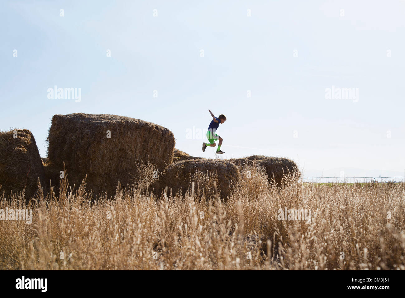 Boy (6-7) jumping on bale of hay Stock Photo - Alamy