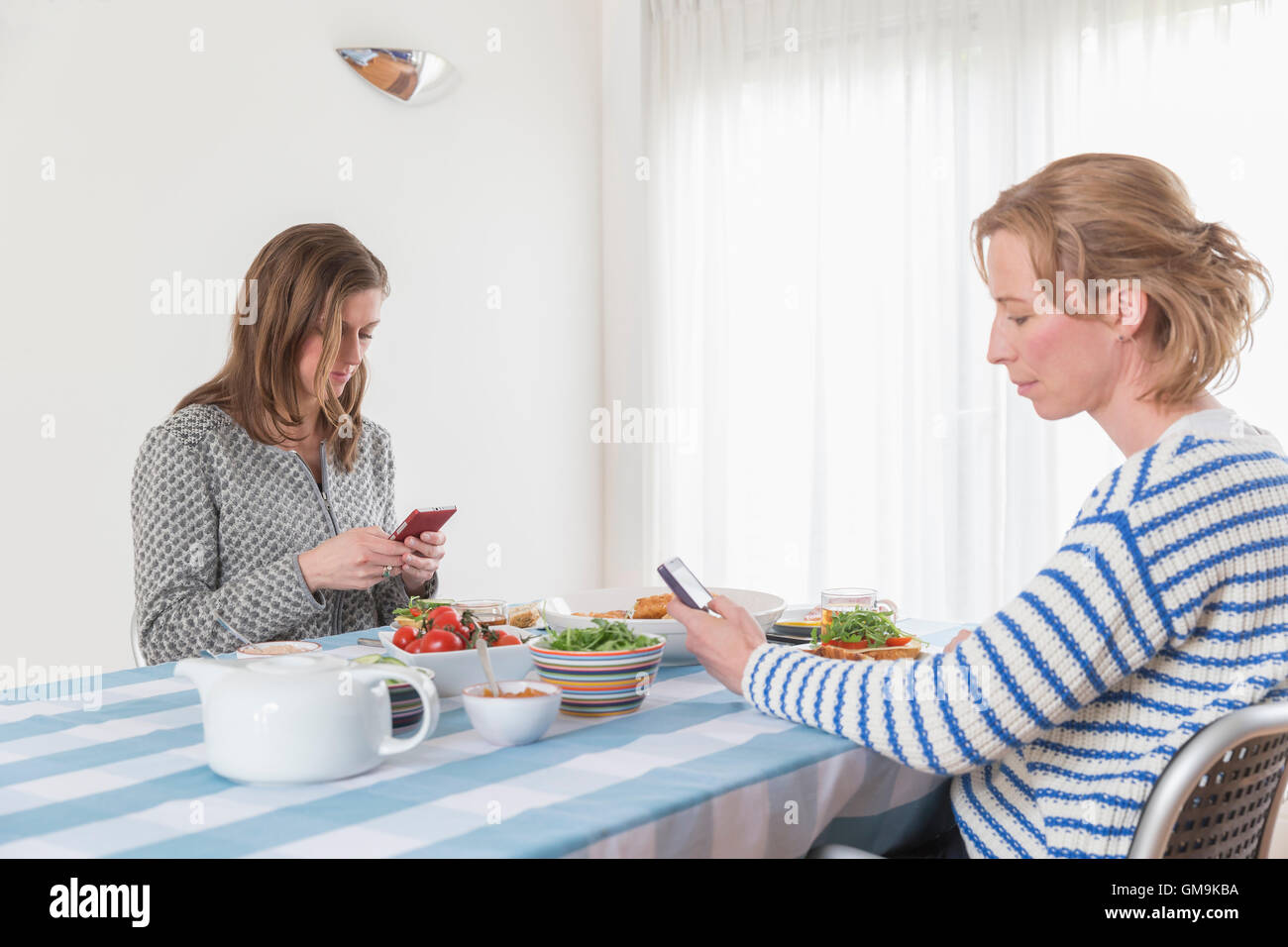 Women checking phones at laid table in dining room Stock Photo - Alamy