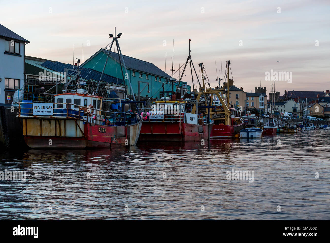 Fishing boats moored along the harbour wall in Aberystwyth at dusk ...