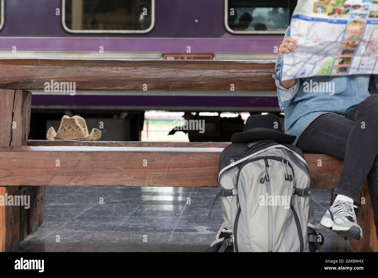 young woman holding map with backpack sitting on platform at train ...