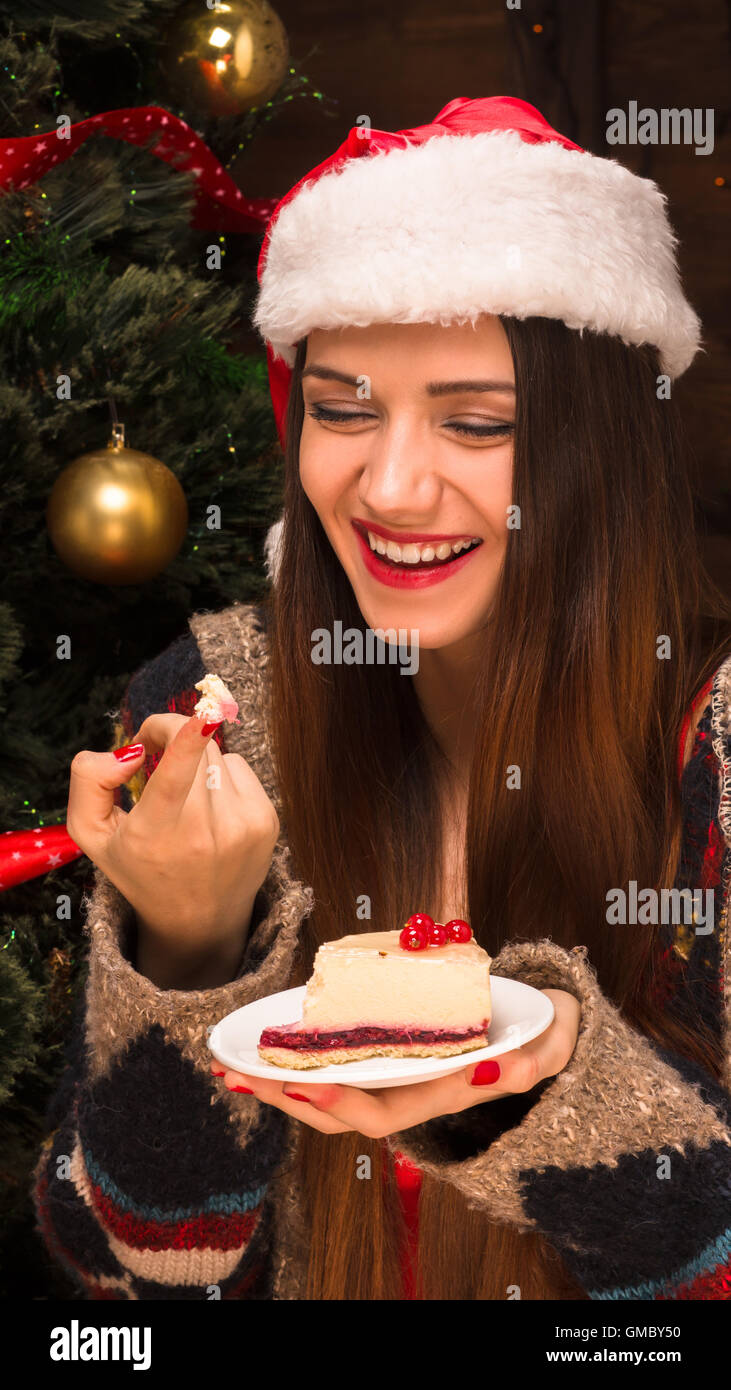 Beautiful girl sitting near New Year tree and eating delicious cake ...