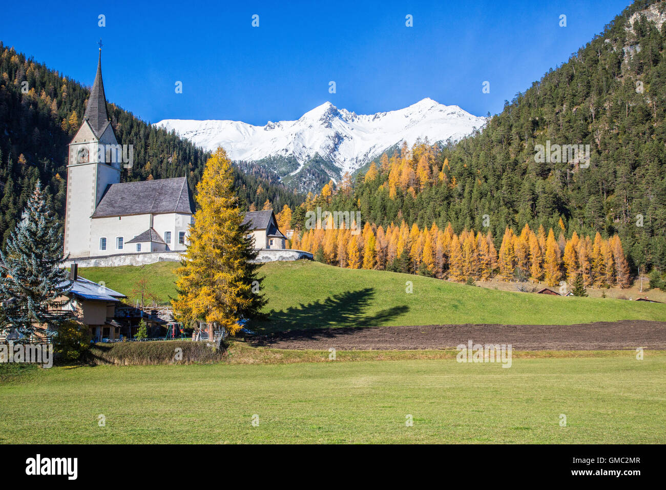 The church of Schmitten surrounded by colorful woods and snowy peaks ...