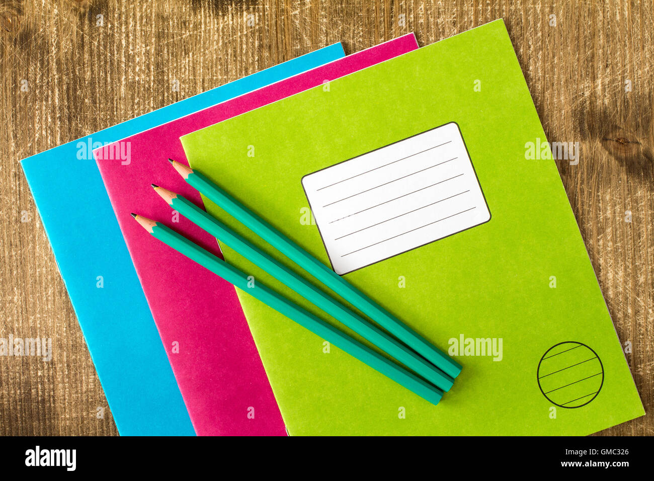 Three colored exercise books and three pencils on the wooden background ...