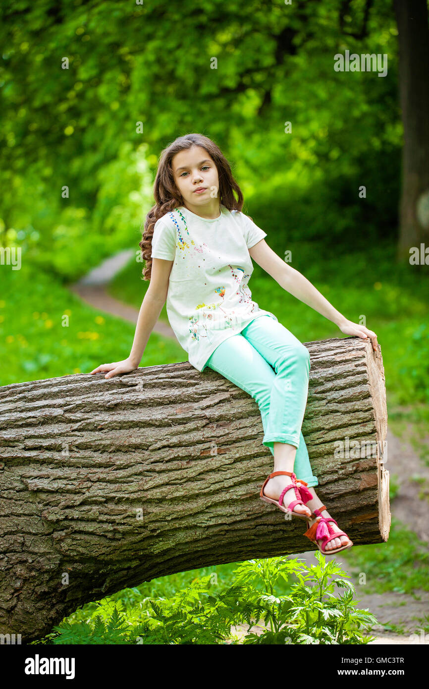 Little Girl in white dress sitting on tree trunk on the background of ...