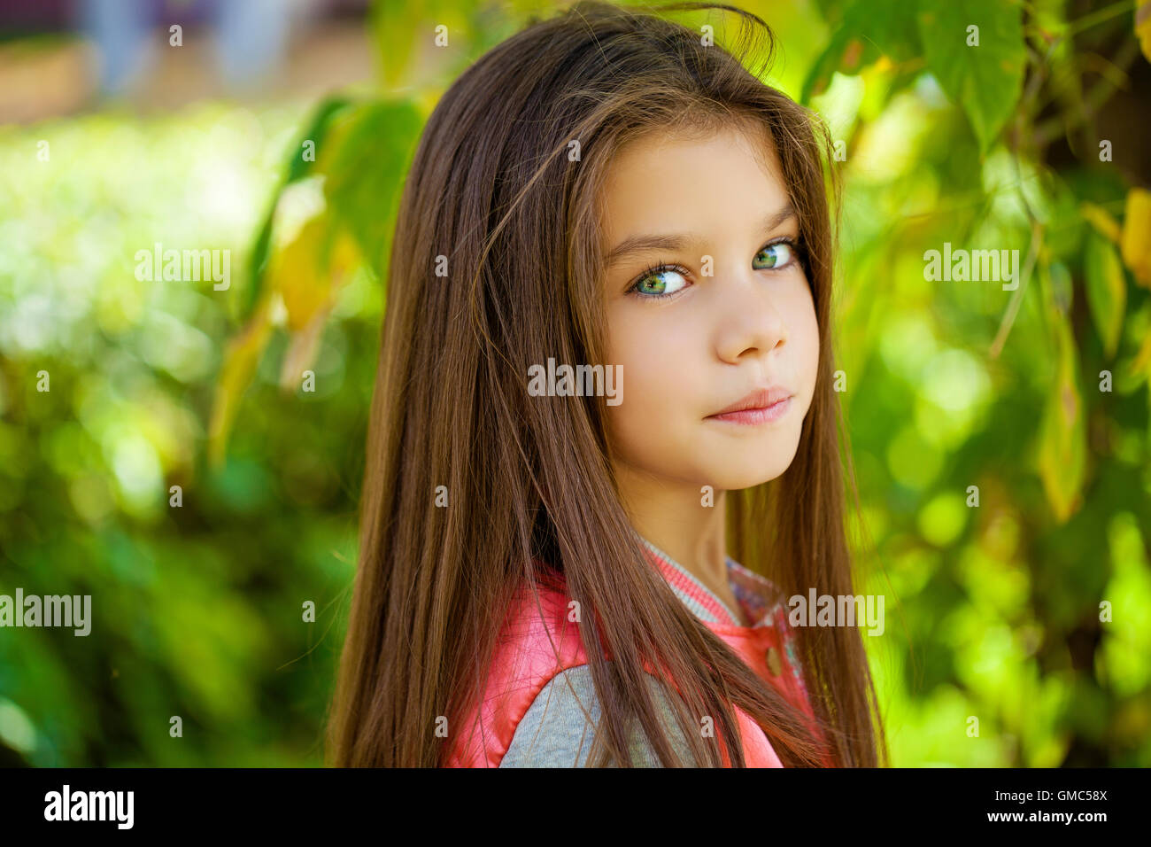 Cose up, Beautiful little girl on green background of summer city park ...