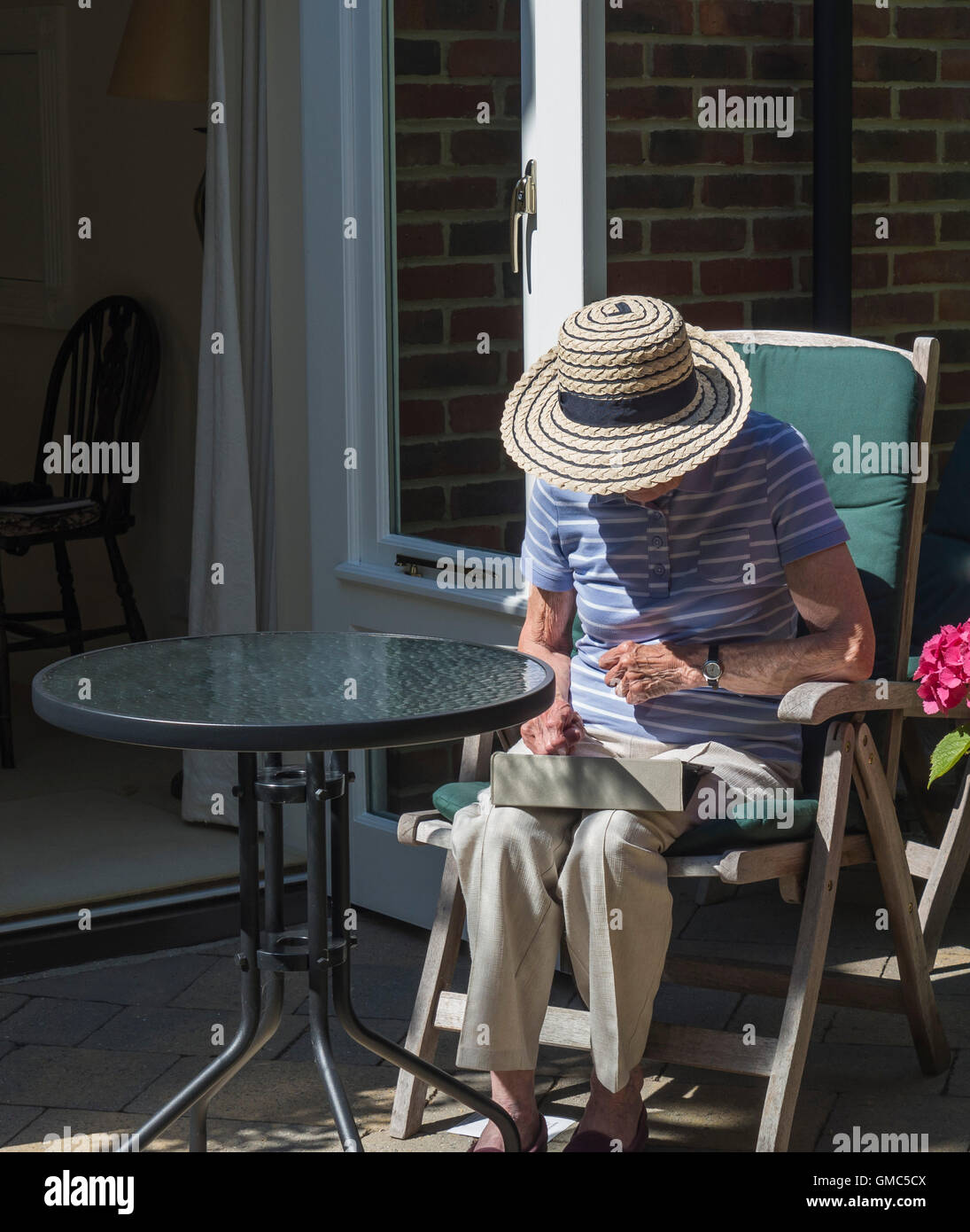 Mature Lady in sun hat sitting outside in a garden reading, UK Stock ...