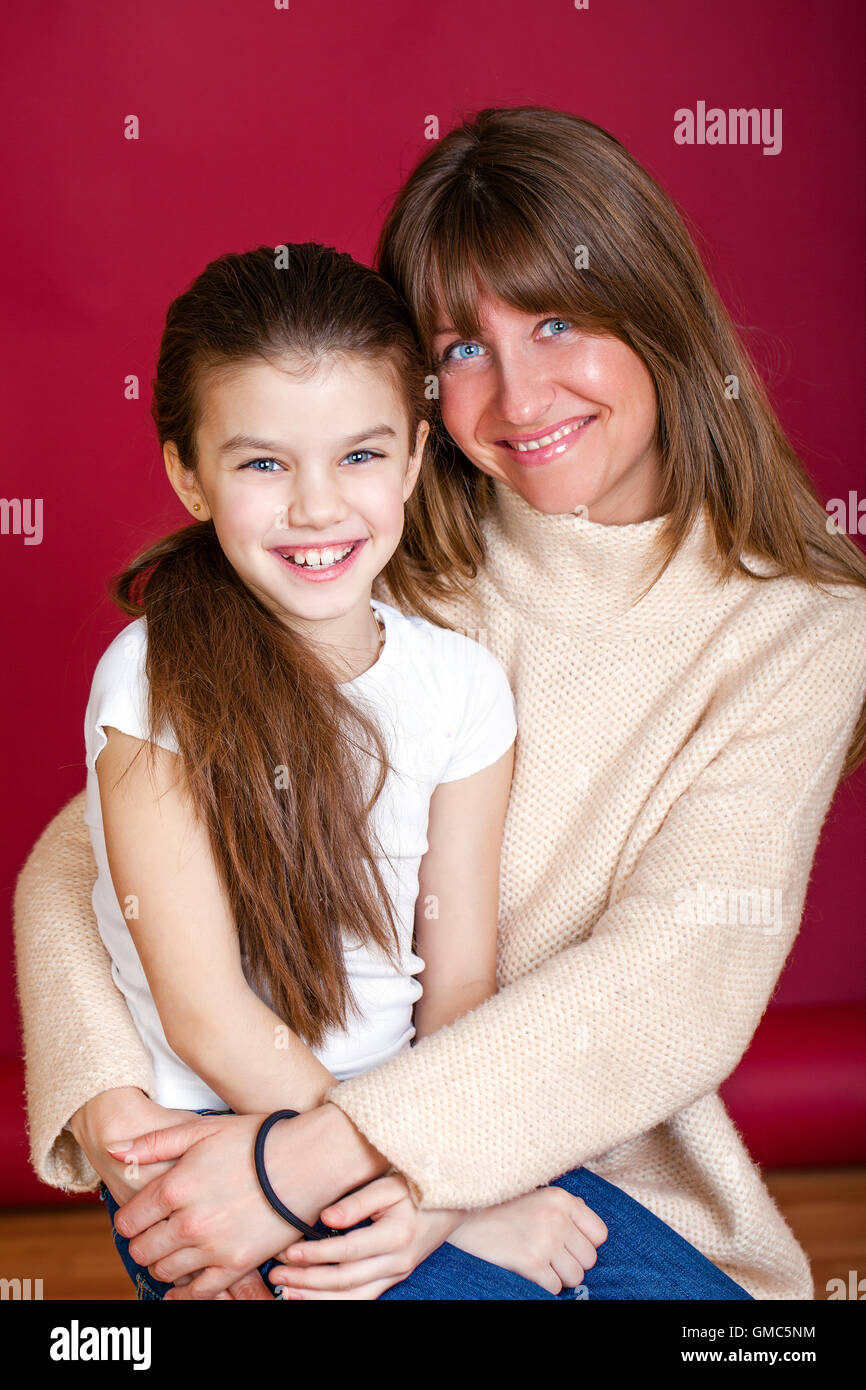 Portrait of seven year old daughter and young mother on red isolated ...