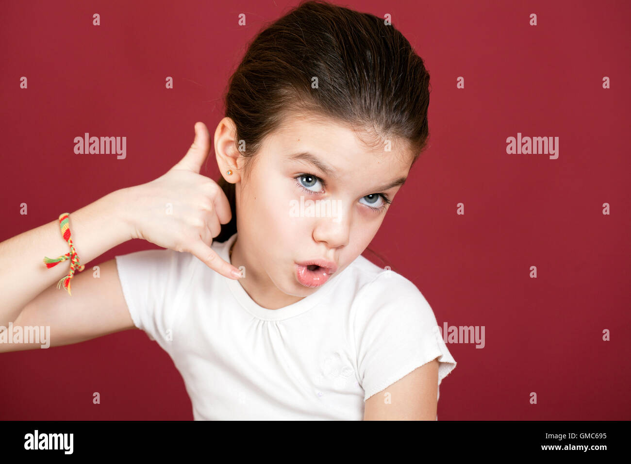 Little Girl making a call me gesture, against background of burgundy ...