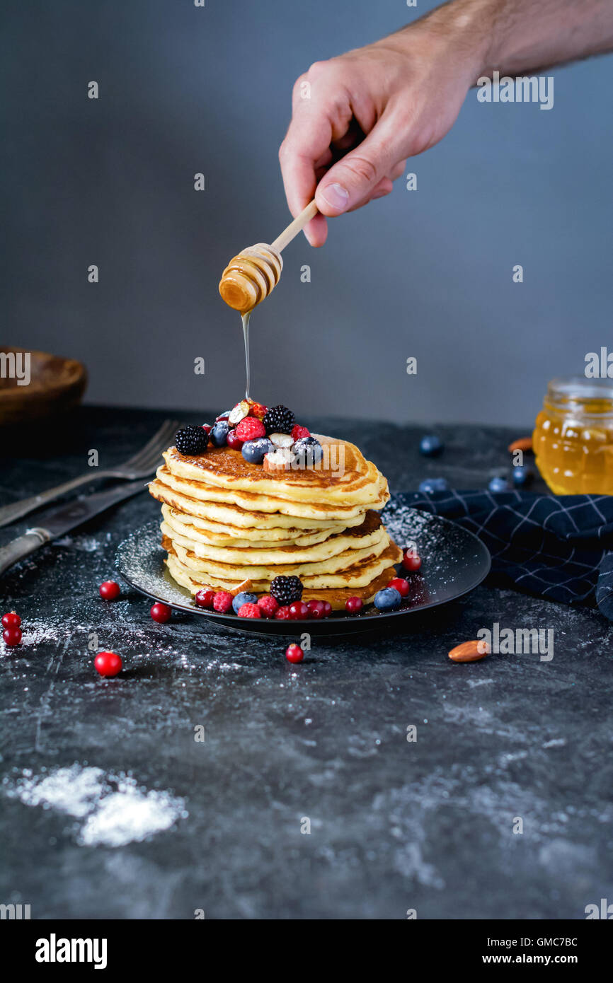 Pancakes for breakfast. Male hand holding honey spoon and pouring honey ...