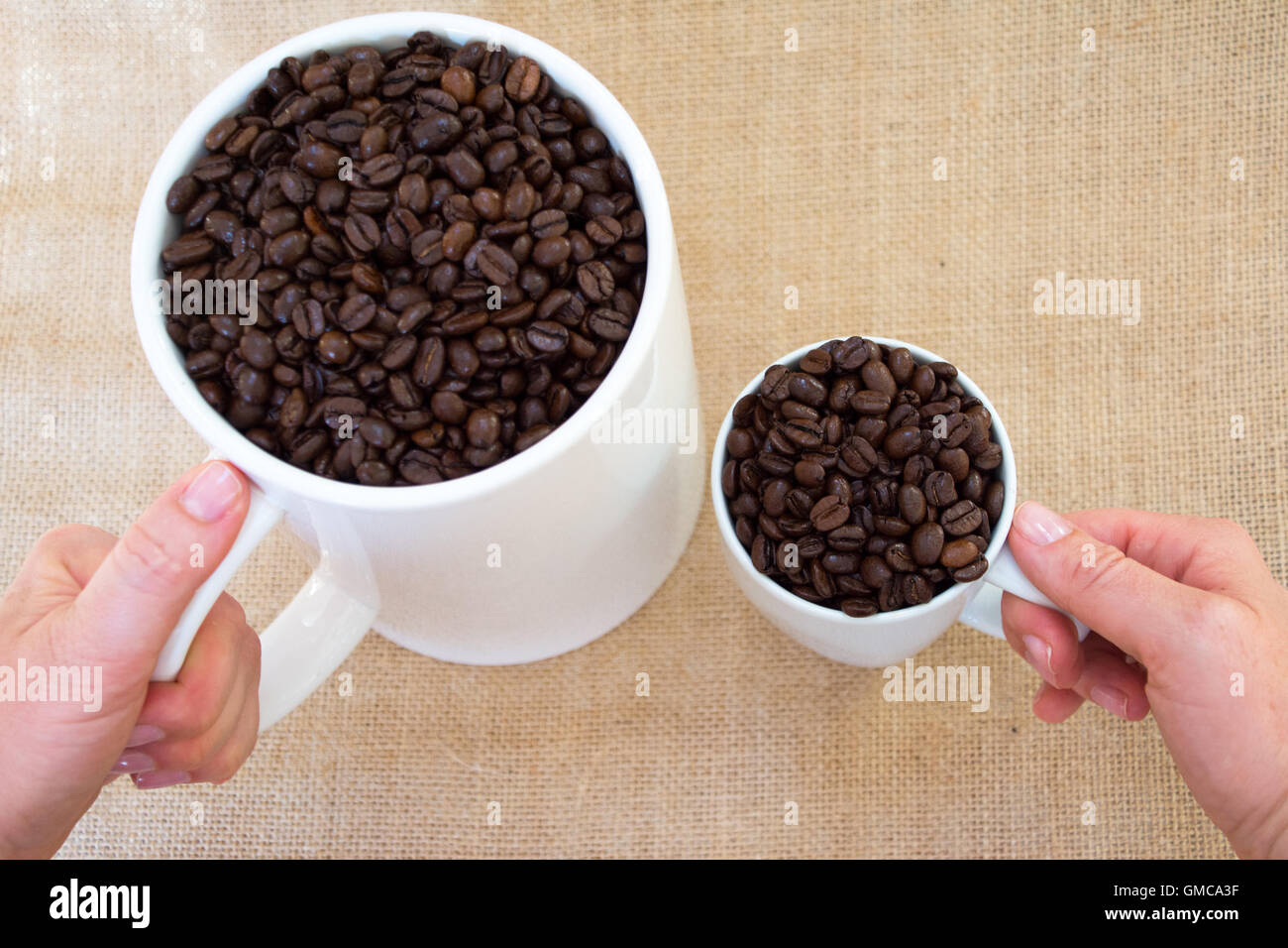 Hand holding Big and Small mugs with coffee beans Stock Photo - Alamy