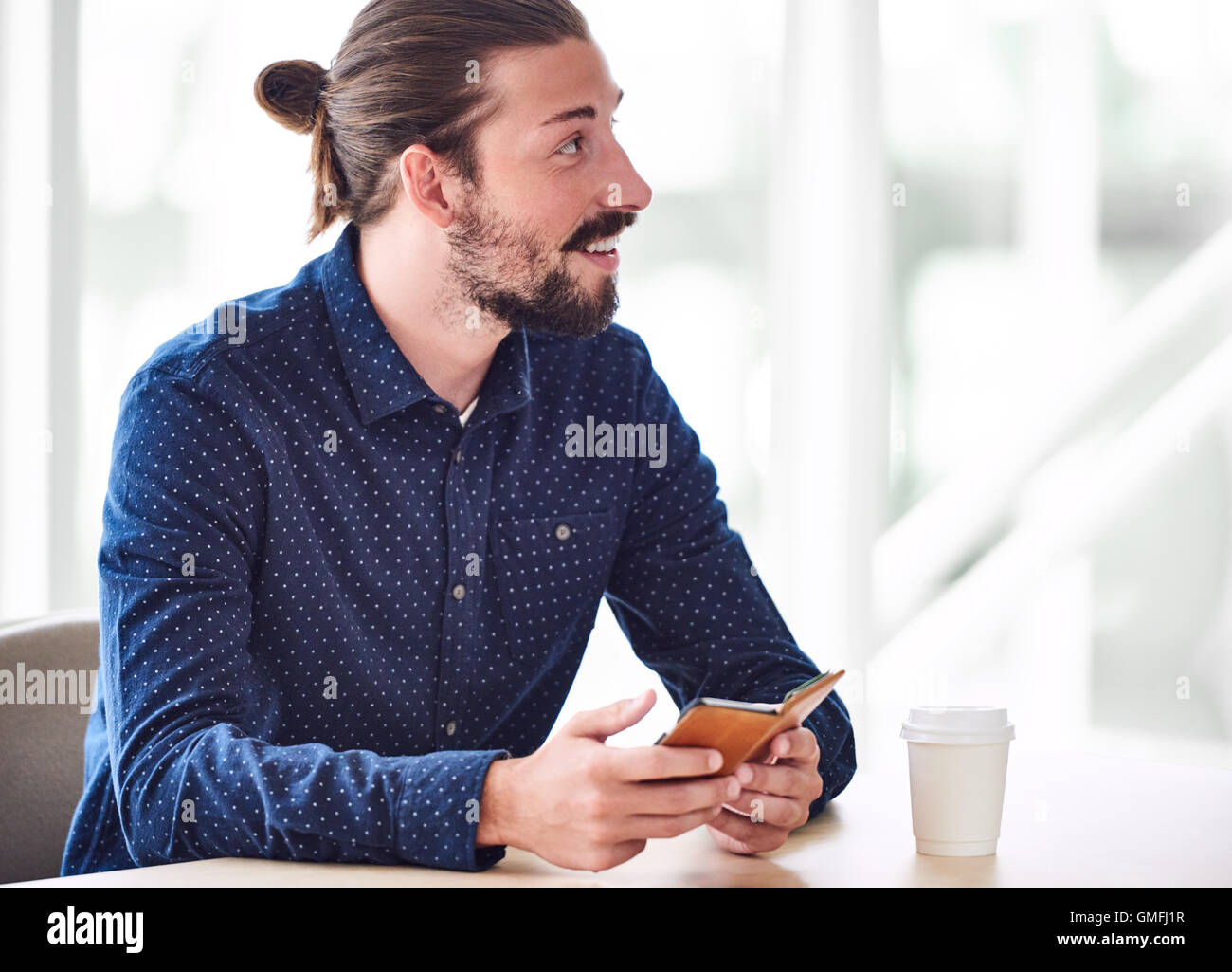 Trendy young man holding phone while looking off camera Stock Photo - Alamy