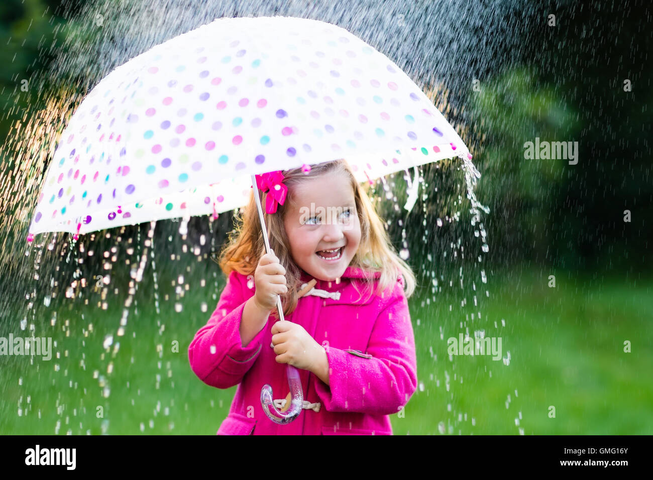 Little girl playing in rainy summer park. Child with colorful rainbow ...