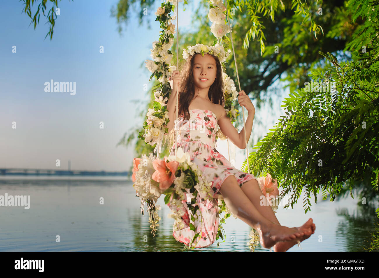 Girl on home made tree swing over river. Swing decorated with flowers ...
