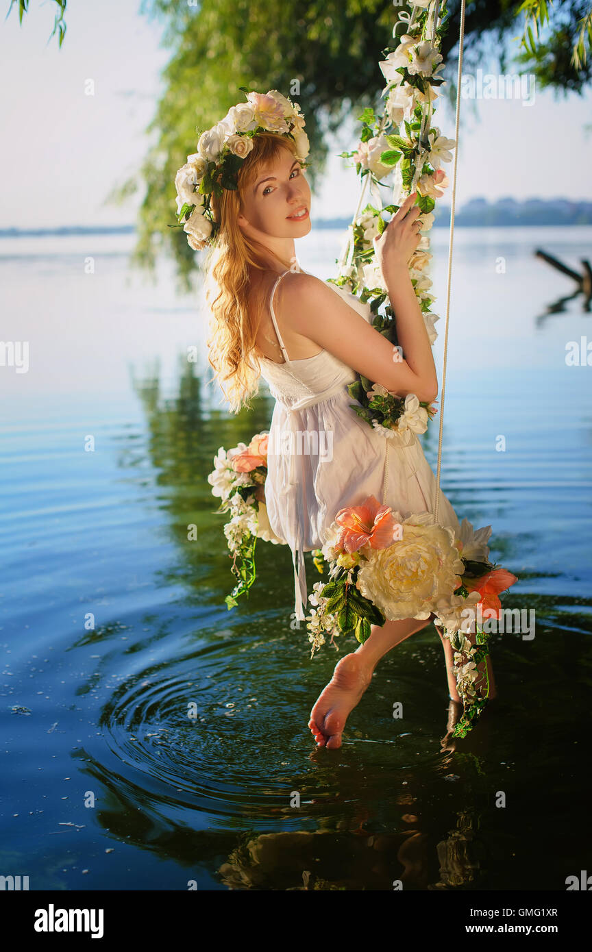 Girl on home made tree swing over river. Swing decorated with flowers ...