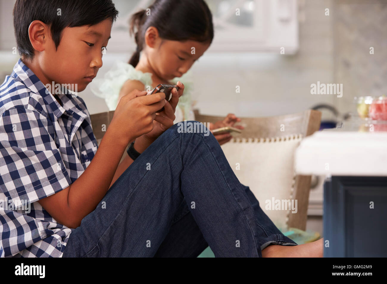 Asian Children Playing Games On Mobile Devices In Kitchen Stock Photo ...