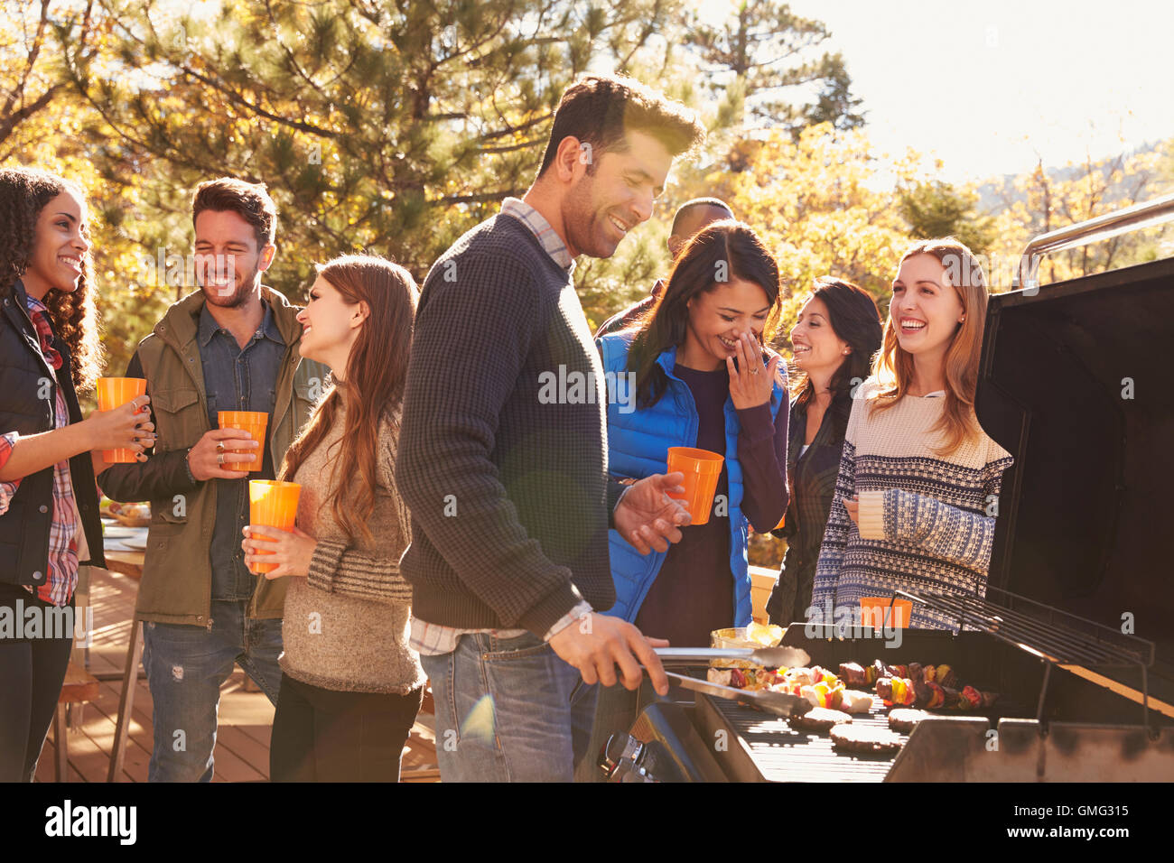 Group of friends stand at a barbecue, one cooking at grill Stock Photo ...
