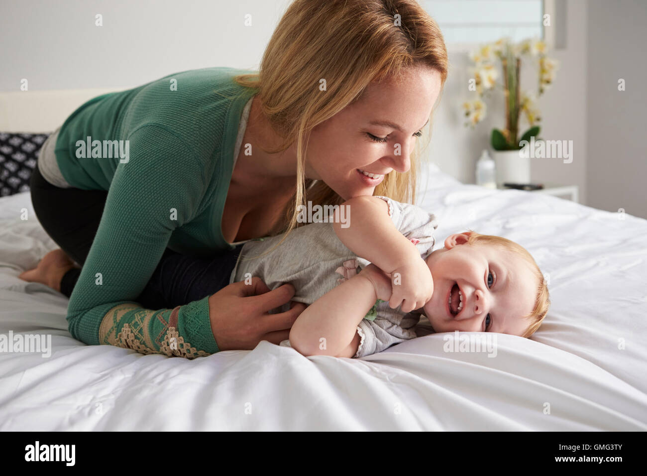 Caucasian mother kneeling on bed, tickling her baby daughter Stock ...