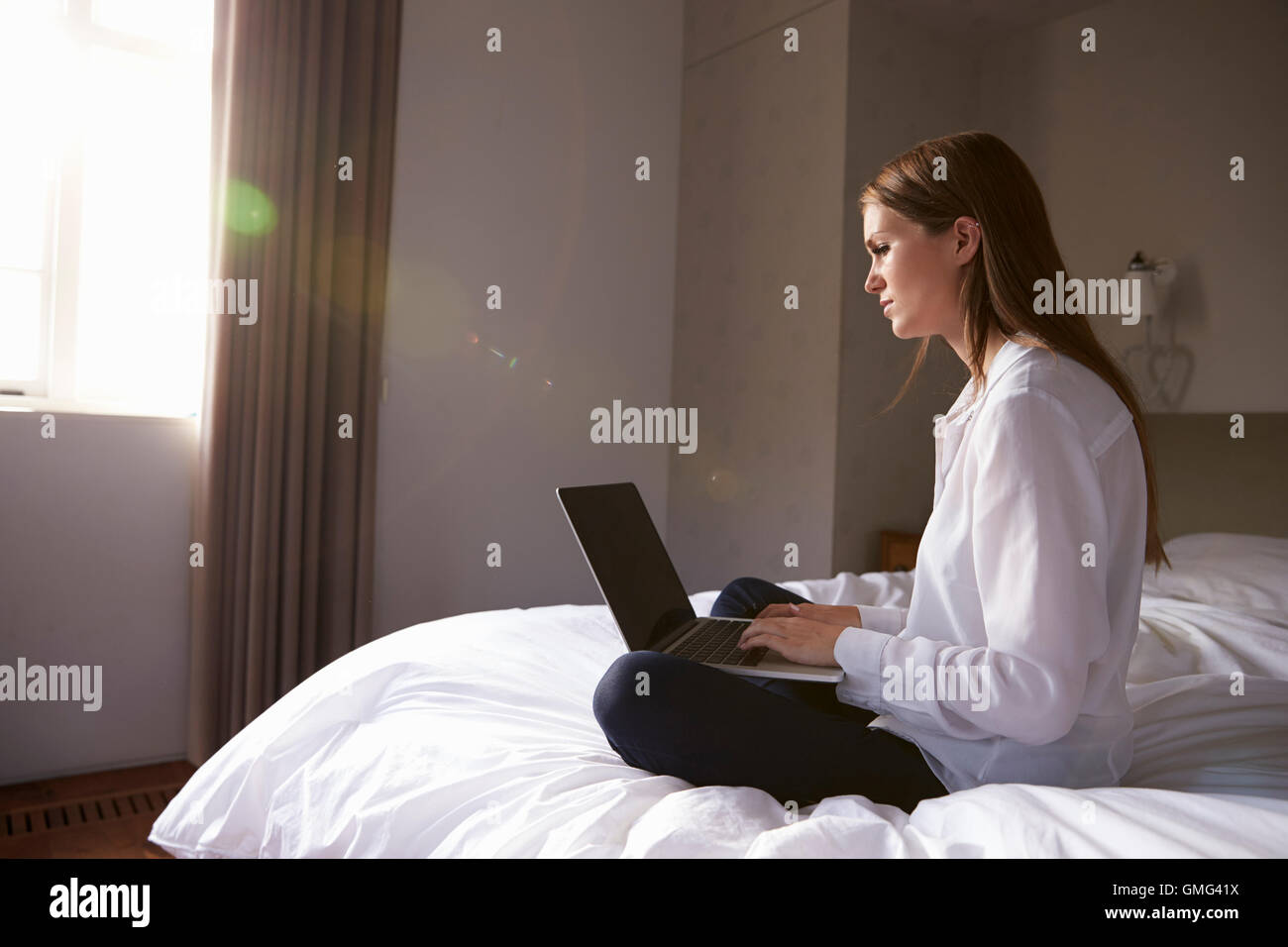 Woman Sitting On Bed In Bedroom Using Laptop Computer Stock Photo - Alamy