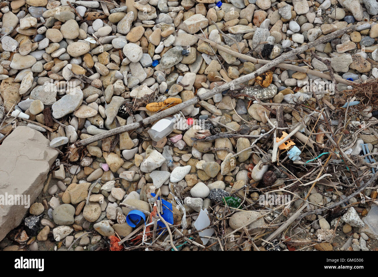 Plastic and driftwood washed ashore on stone beach. Coastal pollution ...