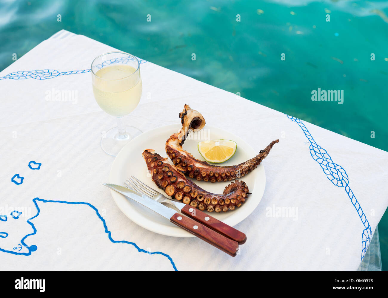 Grilled octopus and white wine glass on a table at the sea coast Stock ...