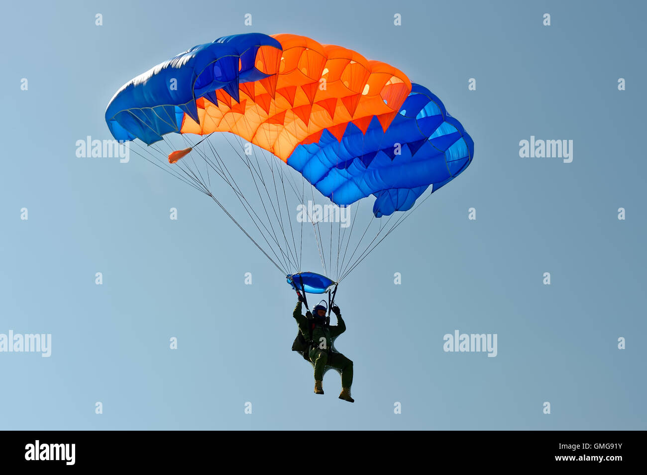Paraglider flying on colorful parachute in blue clear sky at a bright ...