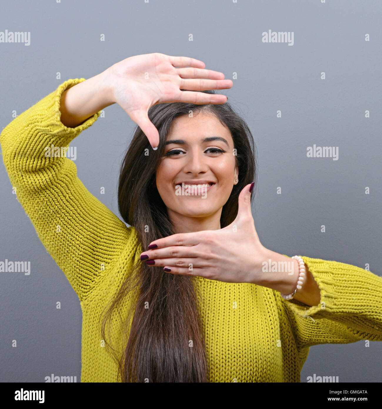Portrait of a young woman making frame with hands against gray background Stock Photo - Alamy
