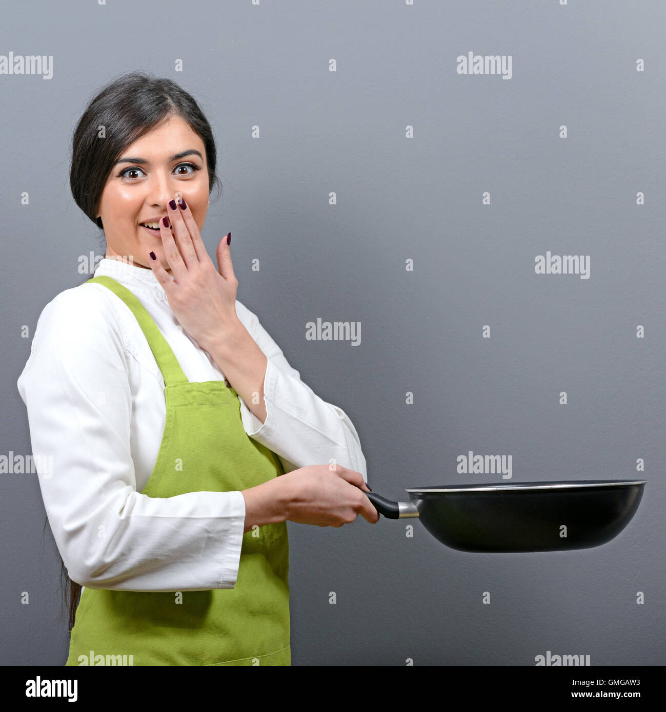 Portrait of beautiful woman chef holding pan against gray background ...