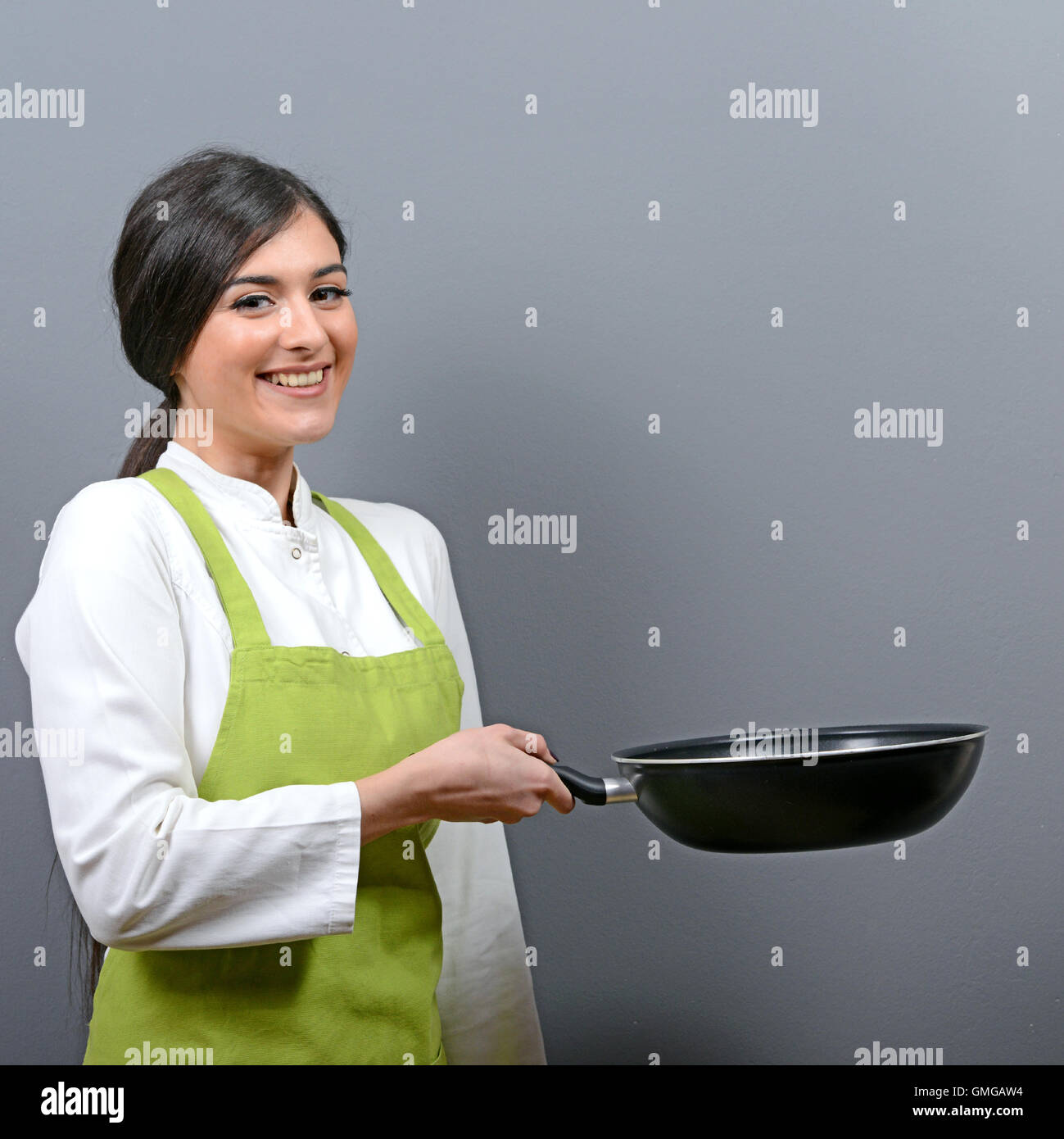 Portrait of beautiful woman chef holding pan against gray background ...