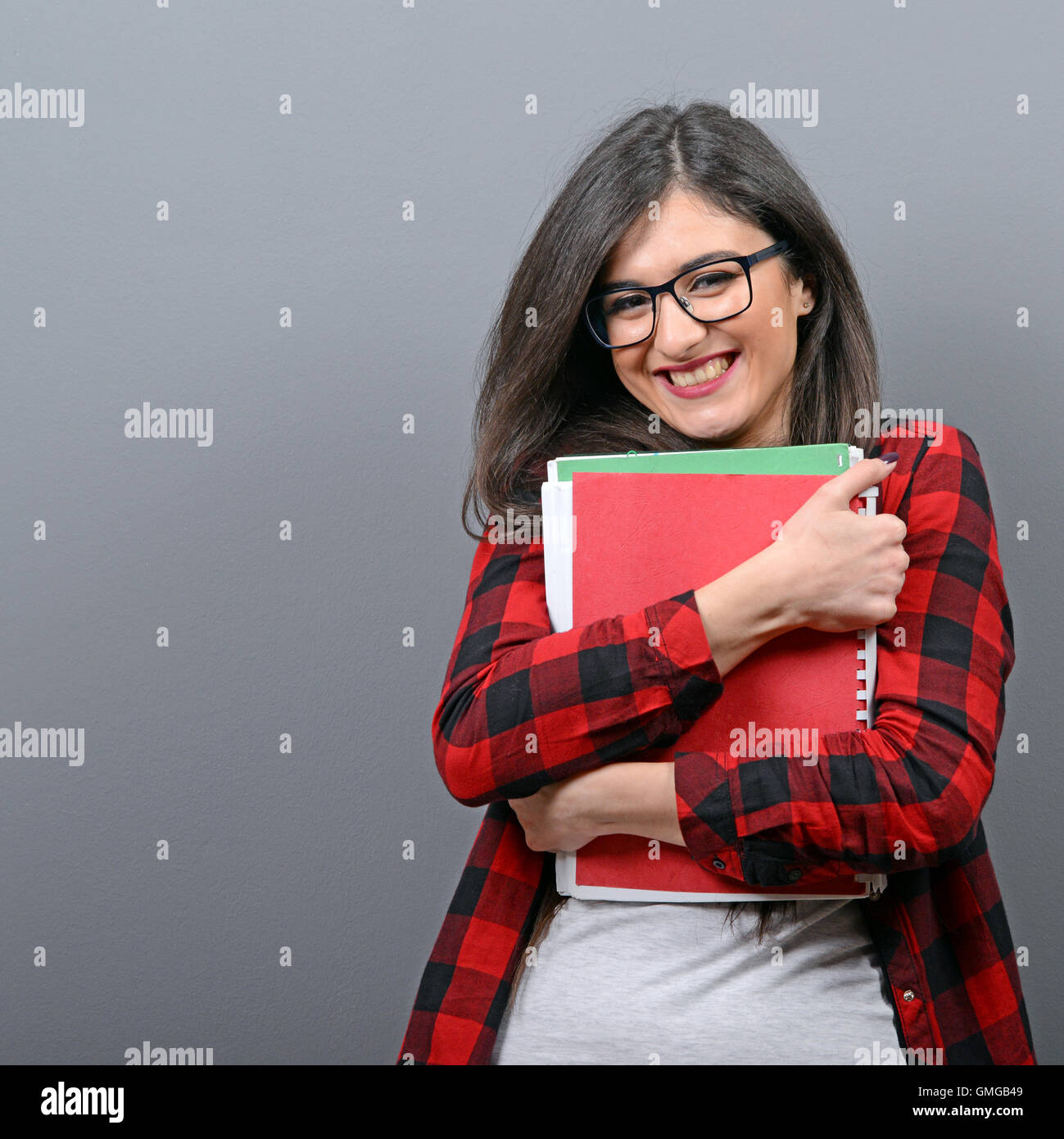 Portrait of happy student woman holding books against gray background ...
