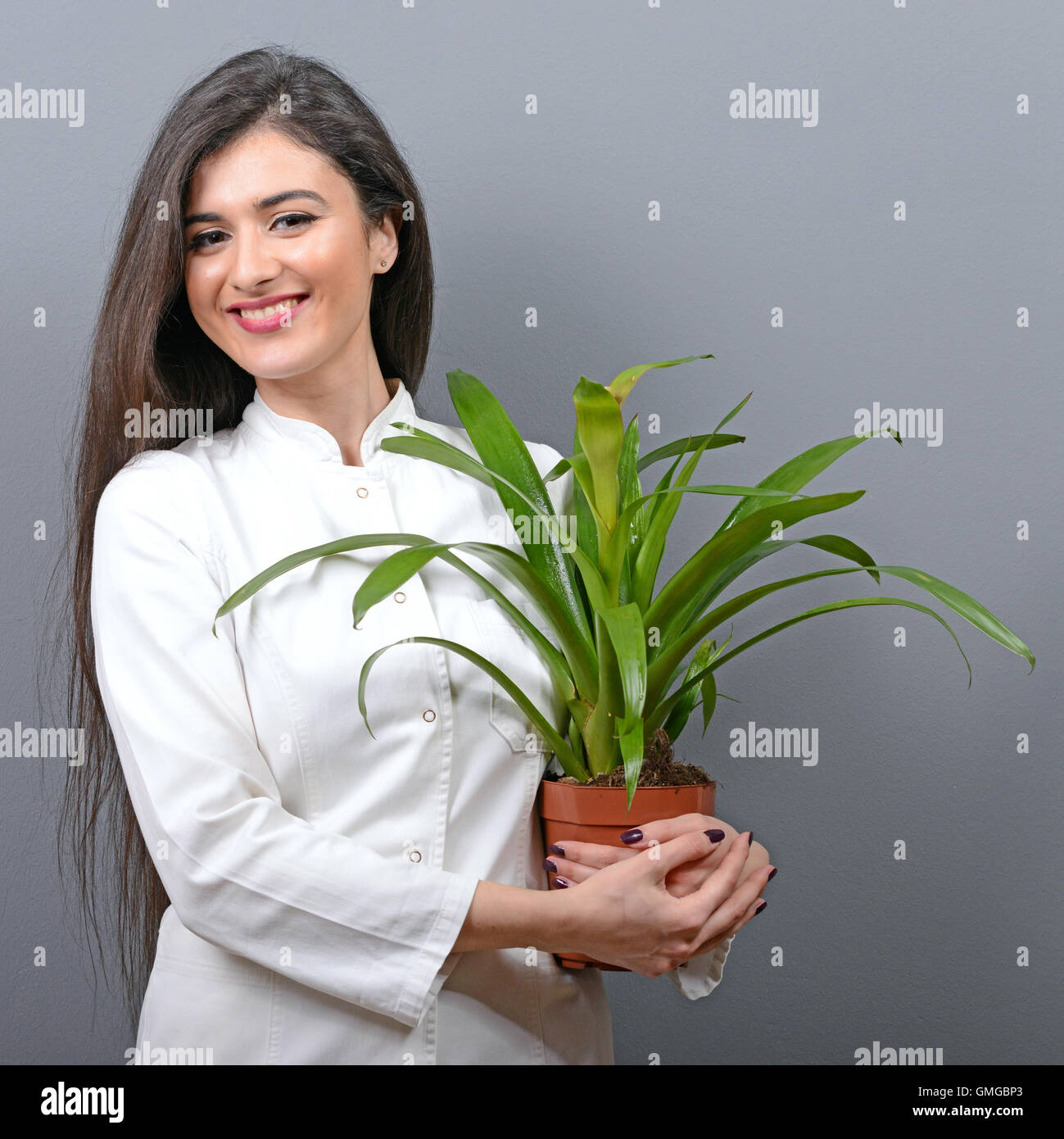 Portrait of young botanist woman in uniform holding plant against gray ...