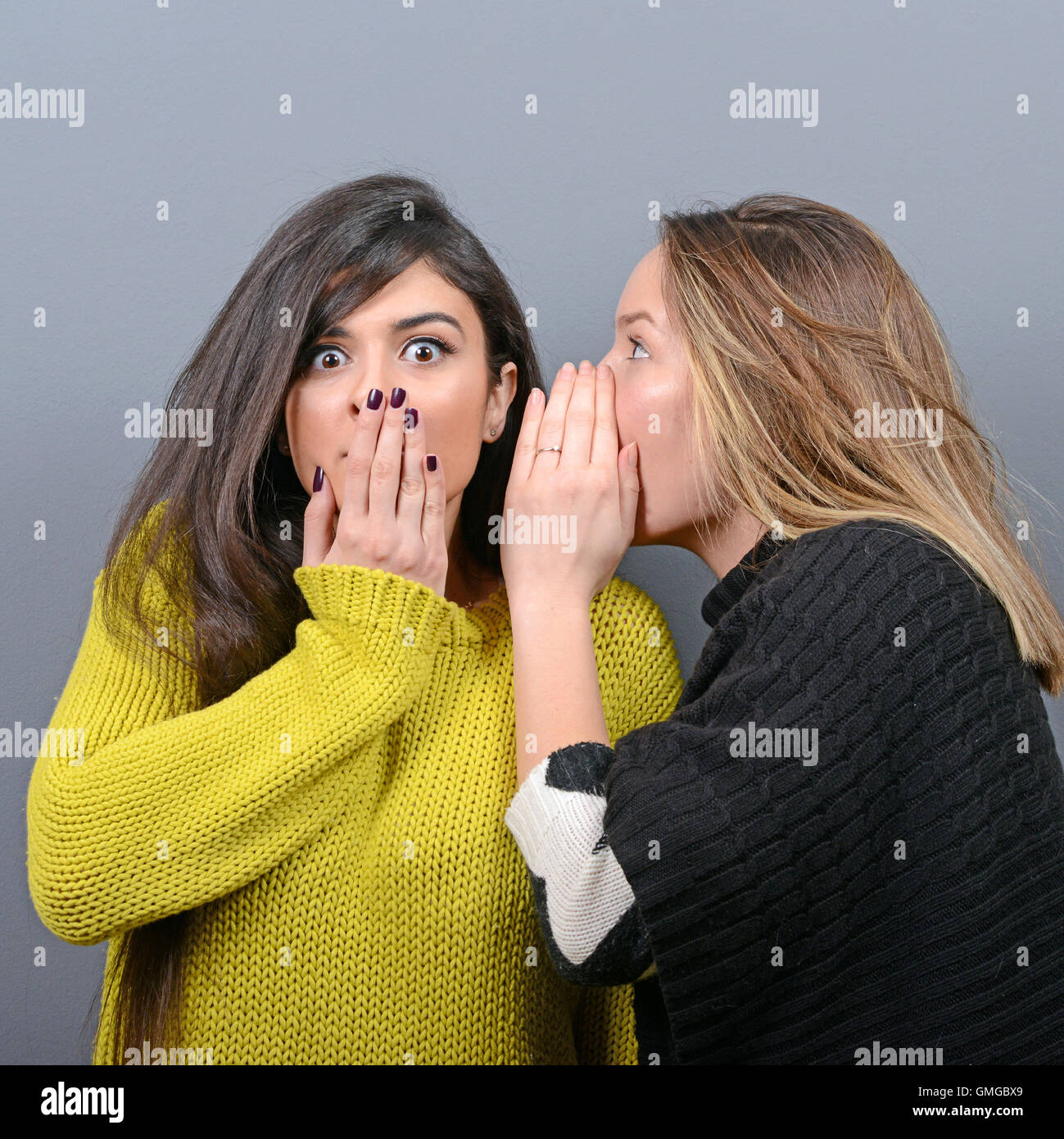 Two woman friends whispering secrets against gray background Stock ...