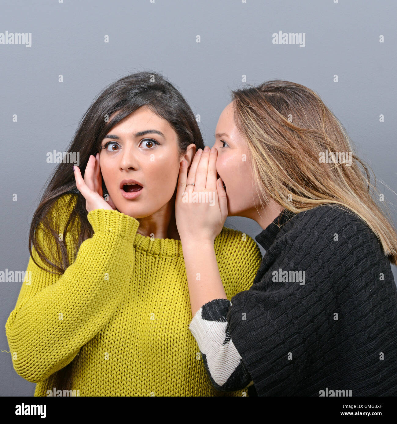 Two woman friends whispering secrets against gray background Stock ...