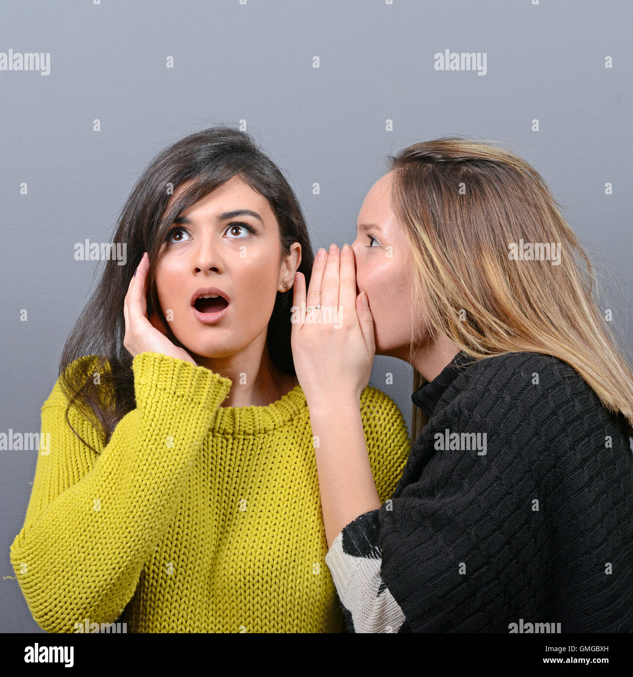 Two woman friends whispering secrets against gray background Stock ...