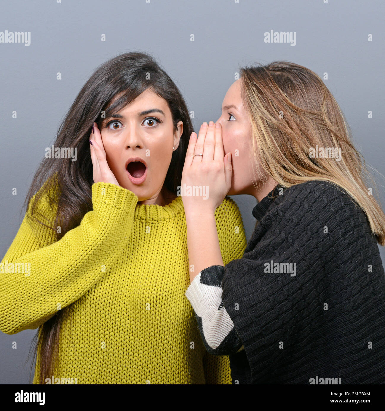Two woman friends whispering secrets against gray background Stock ...