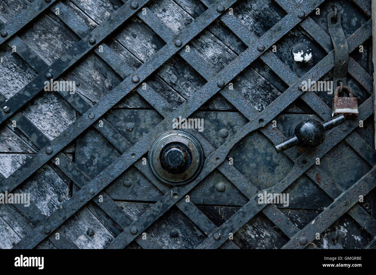 An antique padlock, dial lock and handle on an old iron-fastened door ...