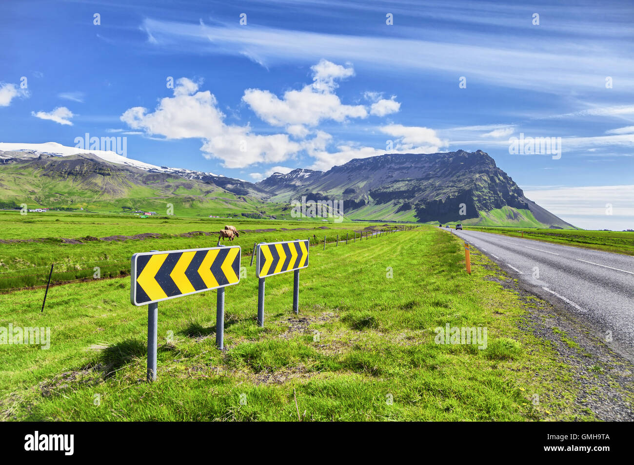 Icelandic landscape with green fields, mountains and arrowed road signs ...