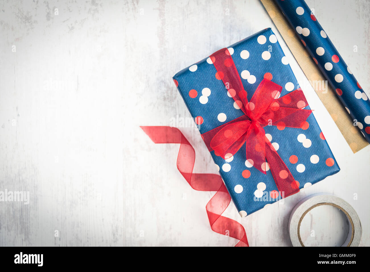 Gift box wrapped in blue dotted paper with red ribbon on a white wood ...